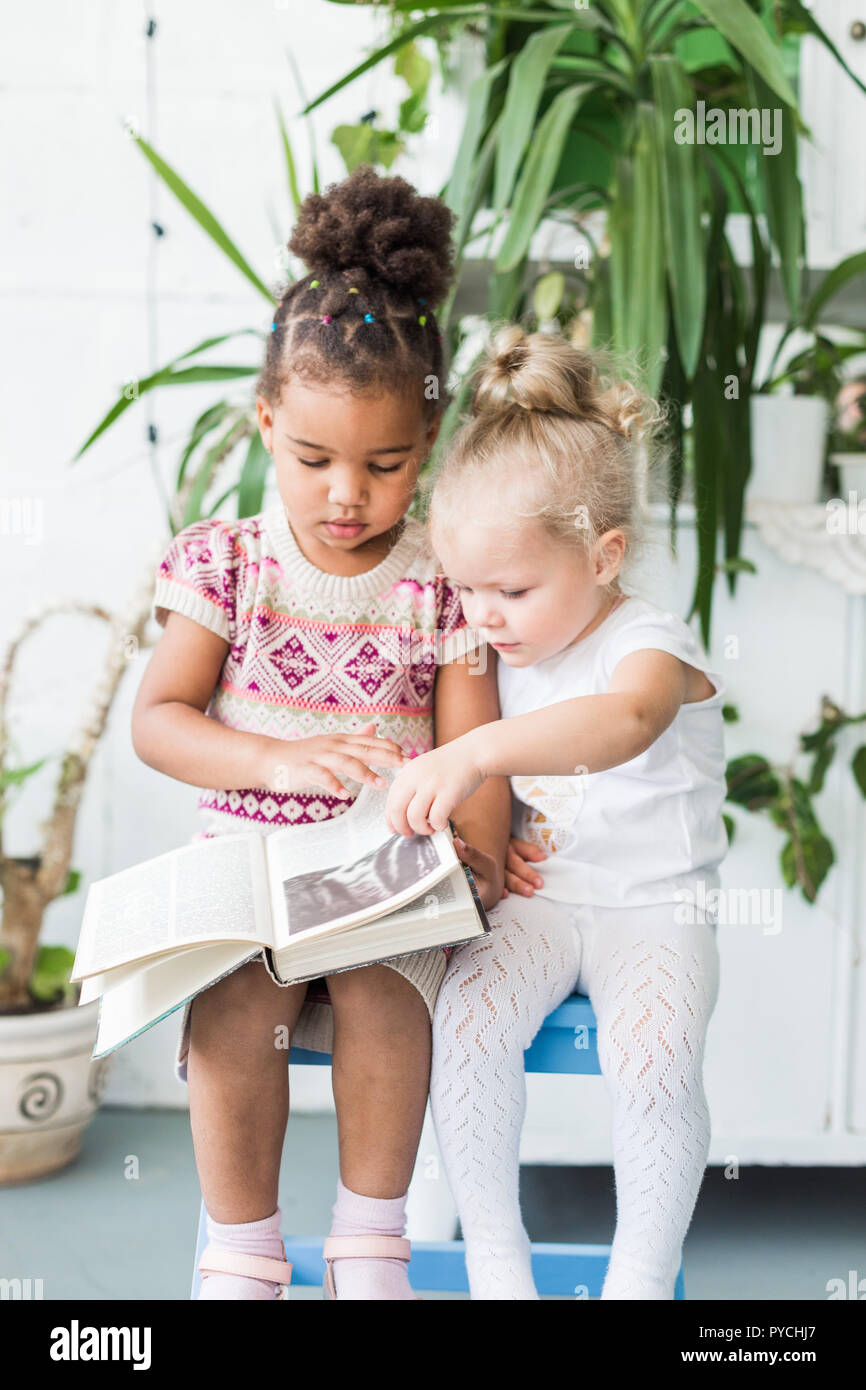 Two little girls read a book on the background of plants in pots ...