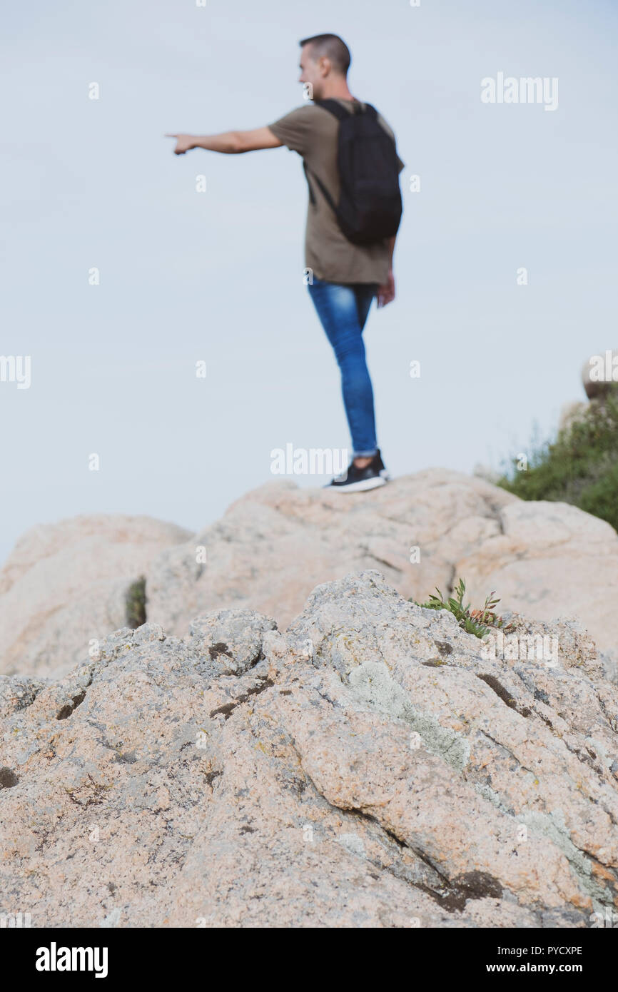 a young caucasian man, carrying a backpack, on the top of a rock ...
