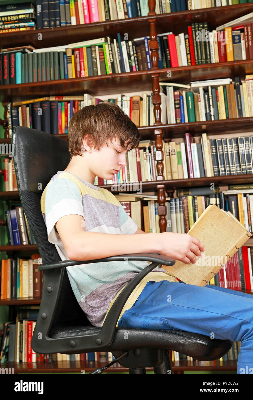 Teenage boy sitting in library and reading book Stock Photo - Alamy