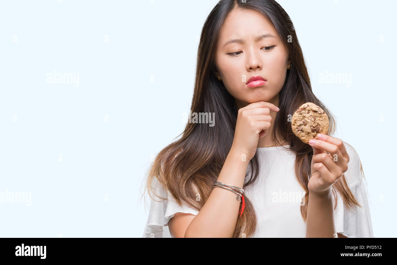 Young asian woman eating chocolate chip cookie over isolated background ...