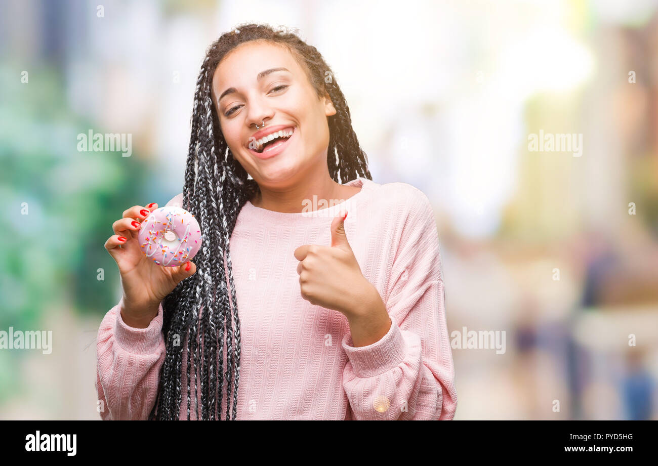 Young african american girl eating pink donut over isolated background happy with big smile ...