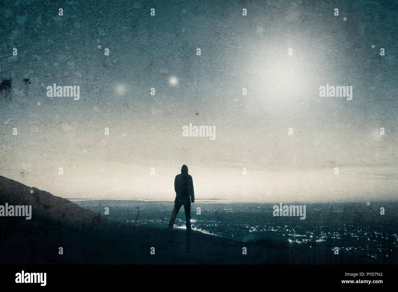 A lone hooded figure looking out across city lights before sunrise as ...