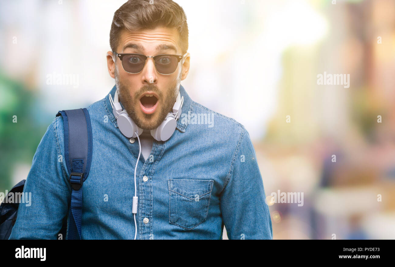 Young handsome tourist man wearing headphones and backpack over isolated background afraid and ...