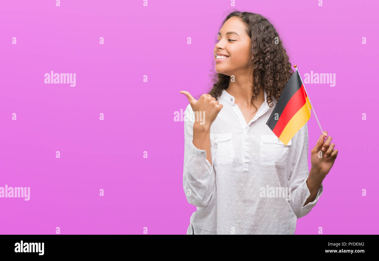 Young hispanic woman holding flag of Germany pointing and showing with ...