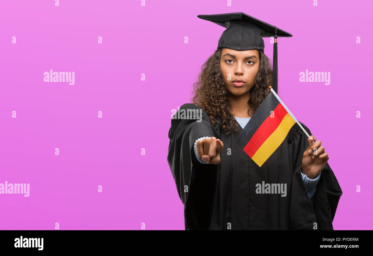 Young hispanic woman wearing graduation uniform holding flag of Germany ...