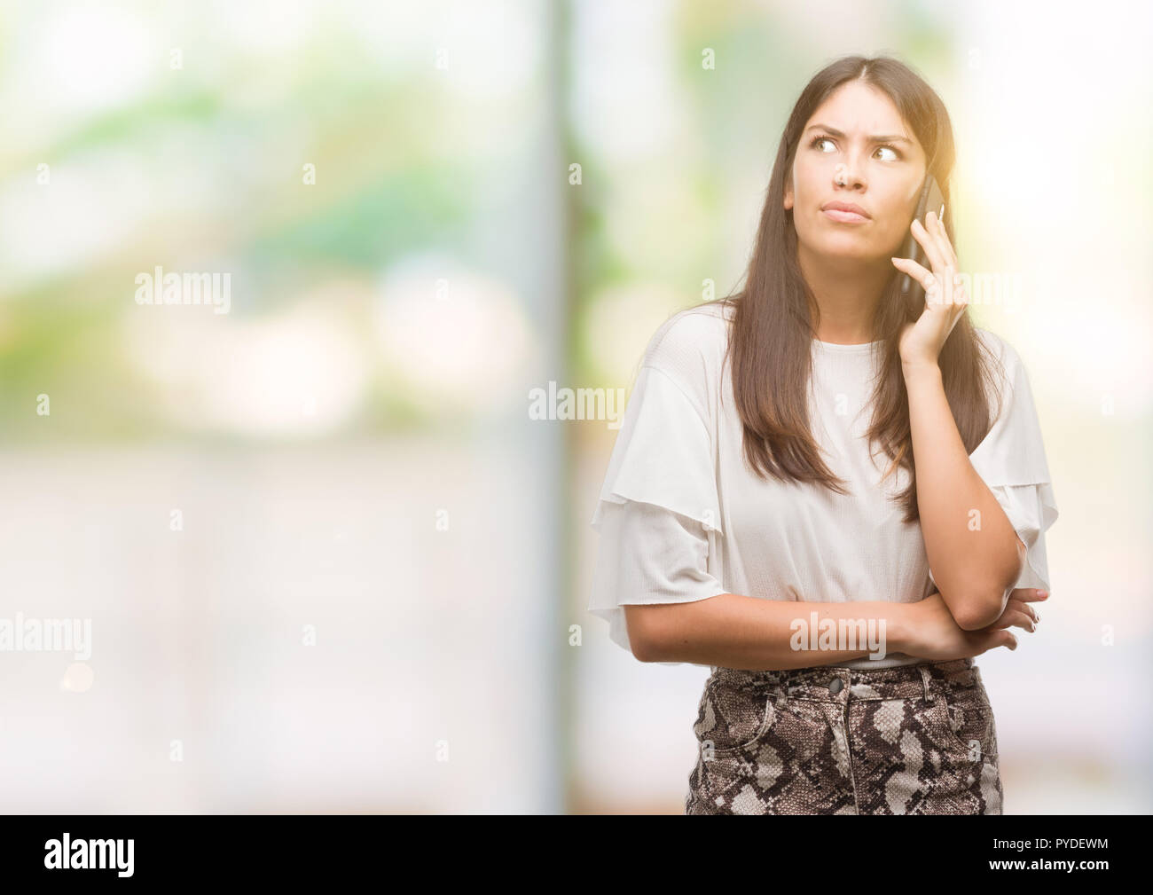 Young beautiful hispanic using smartphone serious face thinking about ...