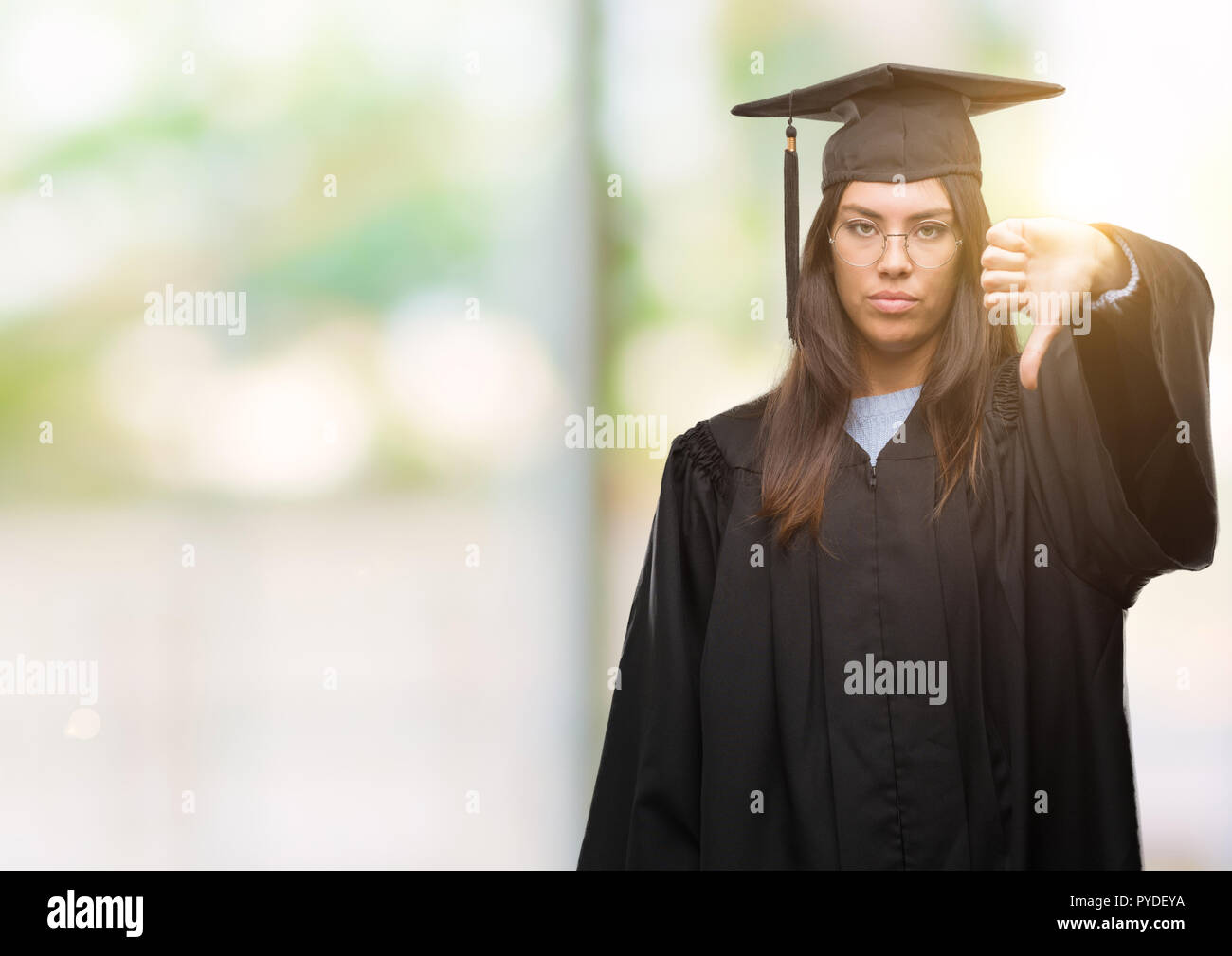 Young hispanic woman wearing graduated cap and uniform looking unhappy ...