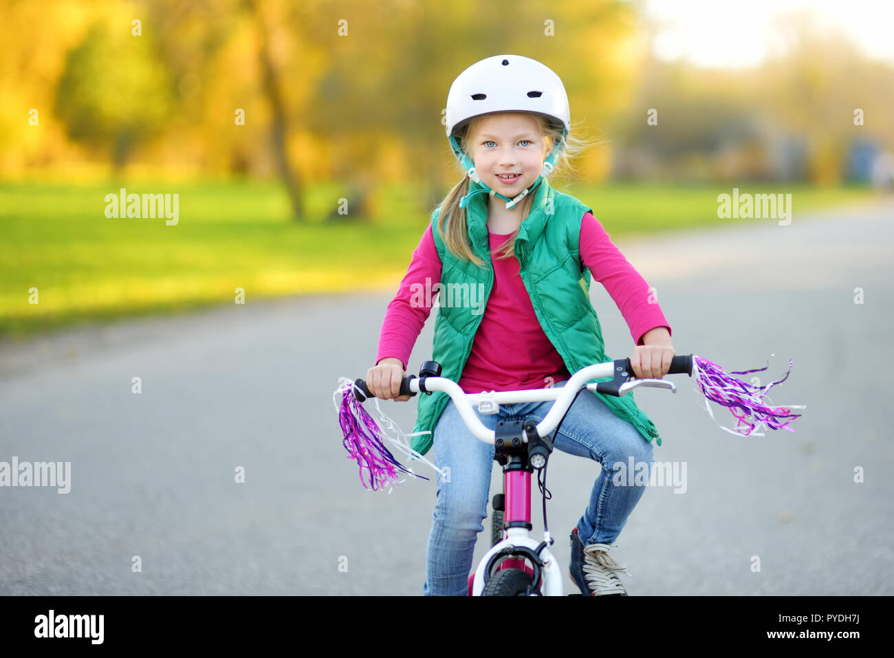 Cute little girl riding a bike in a city park on sunny autumn day ...