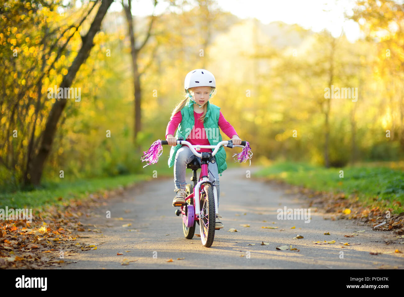 Cute little girl riding a bike in a city park on sunny autumn day ...
