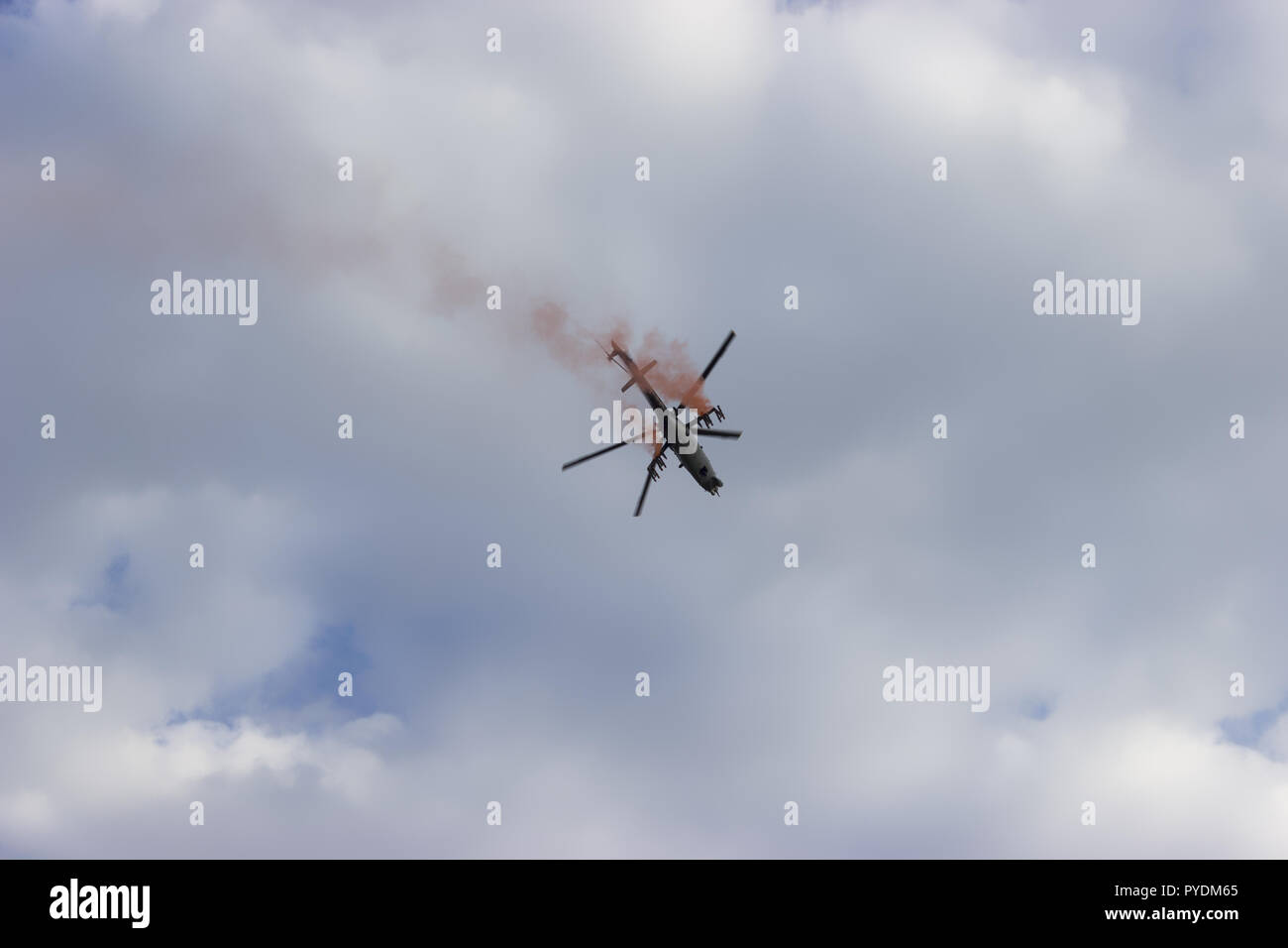 Combat helicopter with red smoke on blue sky with white clouds. View ...