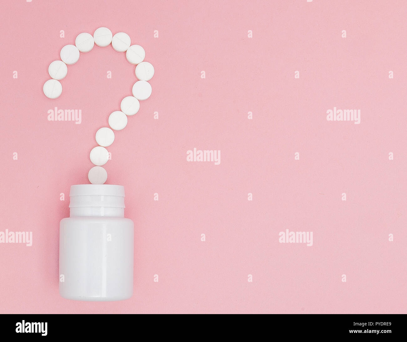 A question mark, laid out of pills and a white plastic bottle on a pink ...