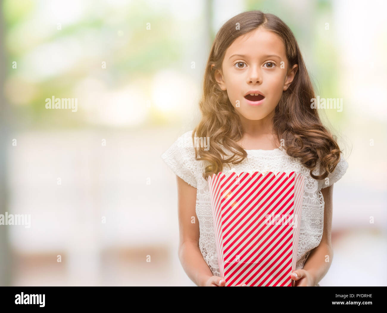 Brunette hispanic girl eating popcorn scared in shock with a surprise ...