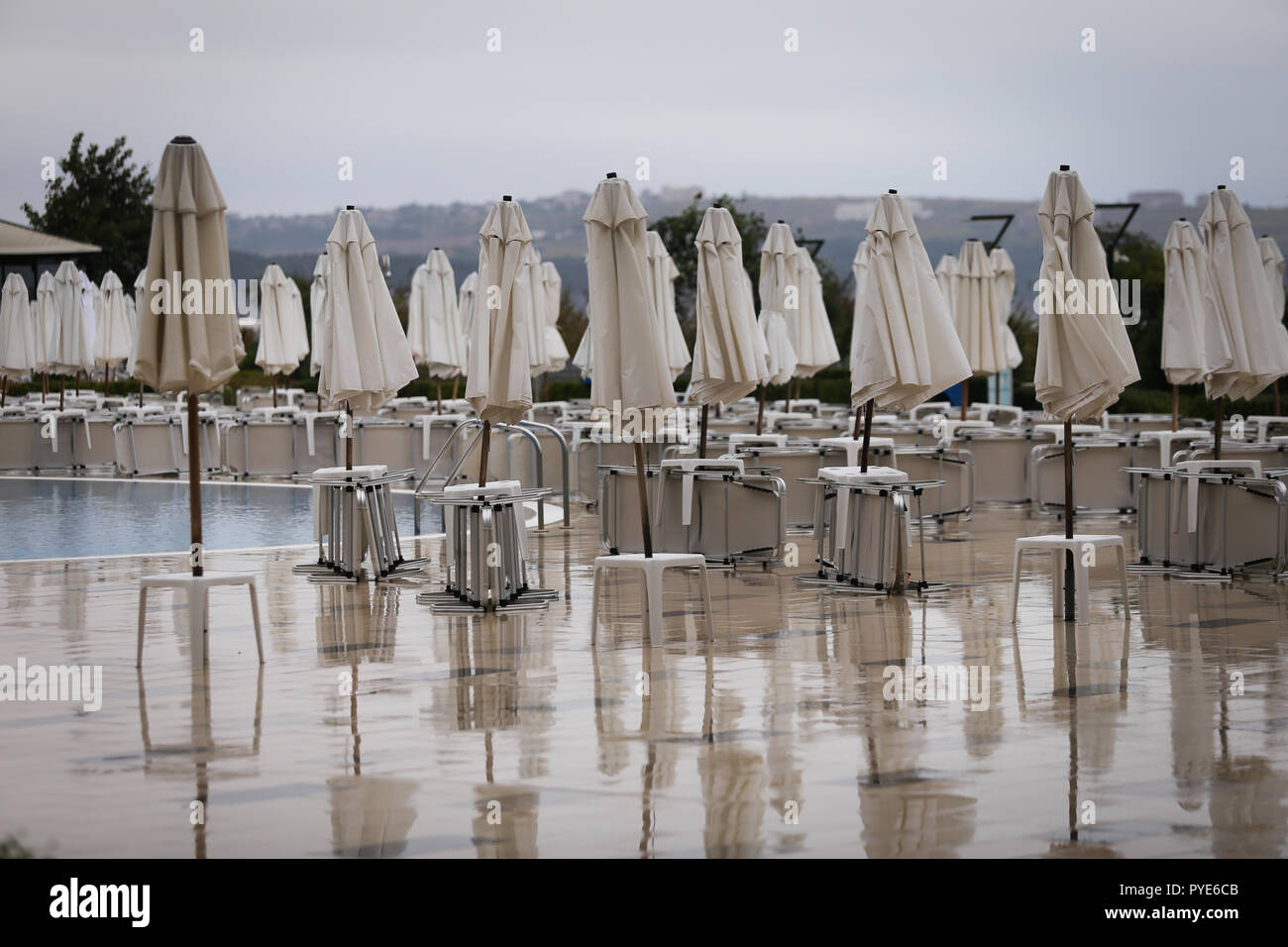 Closed sun umbrellas and lawn chairs around a hotel pool in off season ...