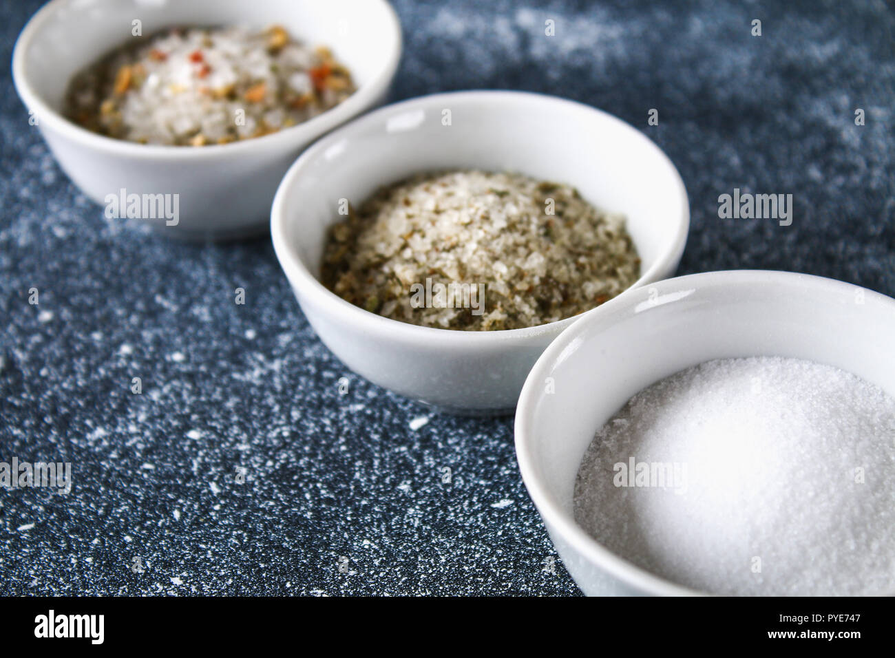 Different types of salt in glass bowls on a dark gray table. Background ...