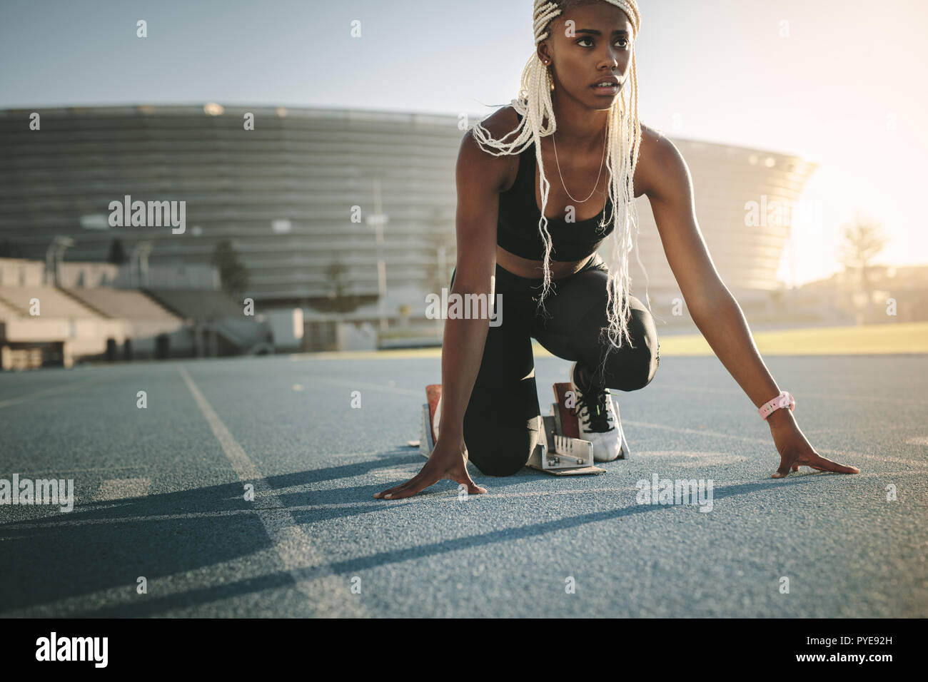 Female athlete taking position on her marks to start off the run ...
