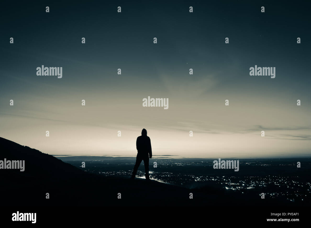 A lone hooded figure looking out across city lights before sunrise as ...