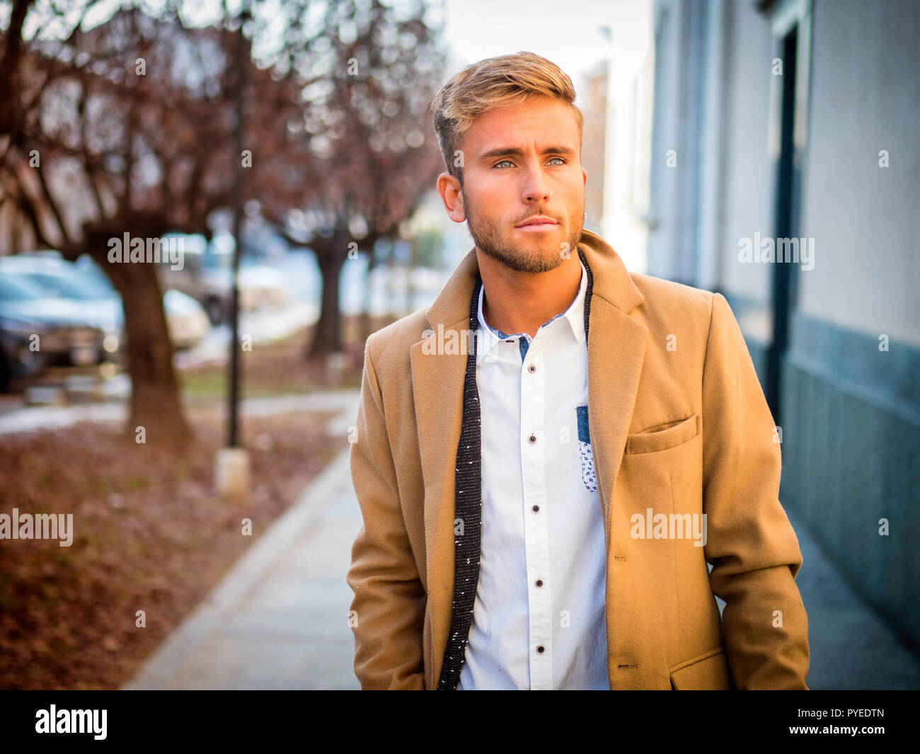 Handsome trendy blond man standing outdoor in European city setting ...