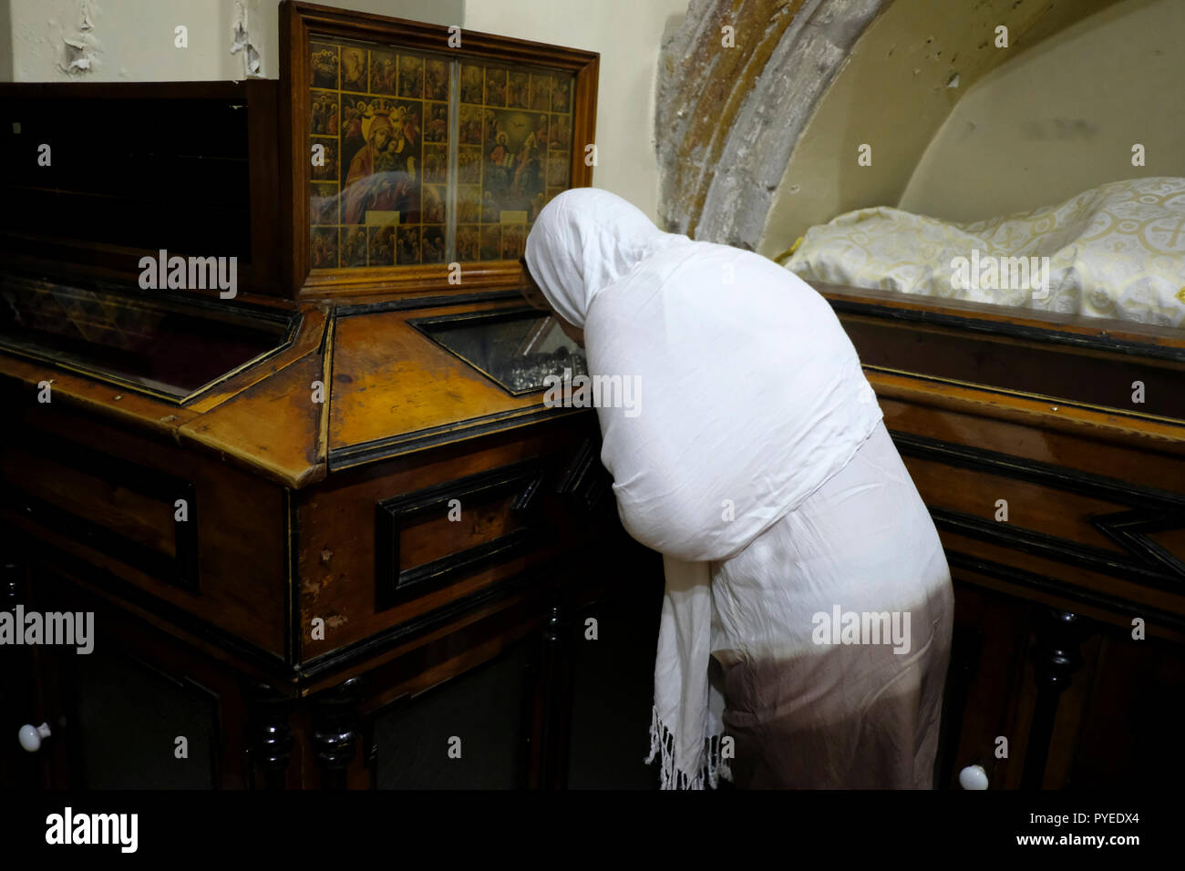 An eastern orthodox pilgrim prays over a wooden reliquary case ...