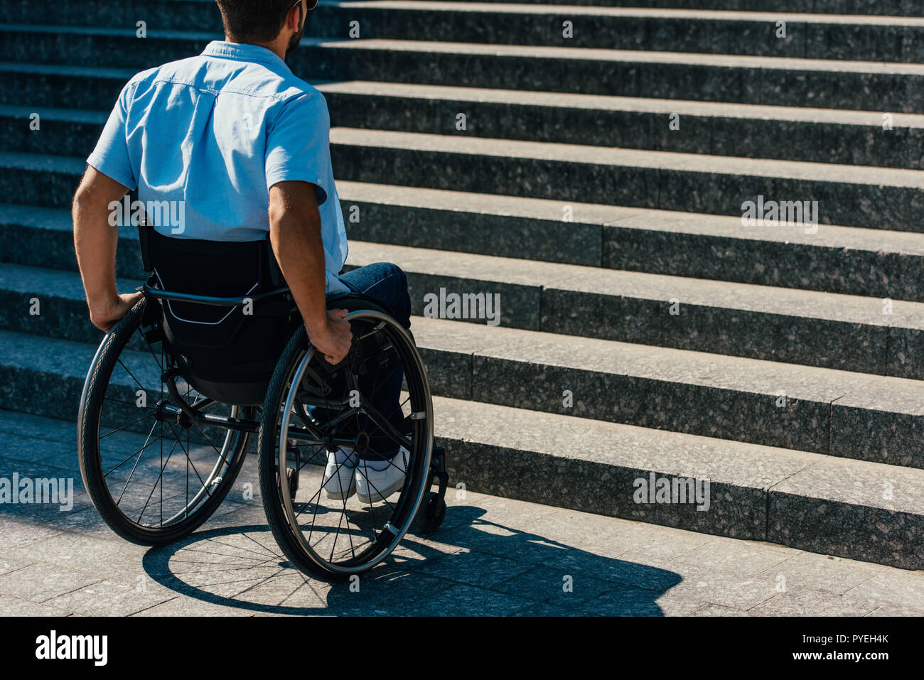 back view of disabled man using wheelchair on street and stopping near ...