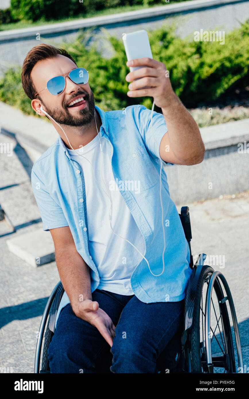 handsome man in wheelchair sticking tongue out and taking selfie with ...