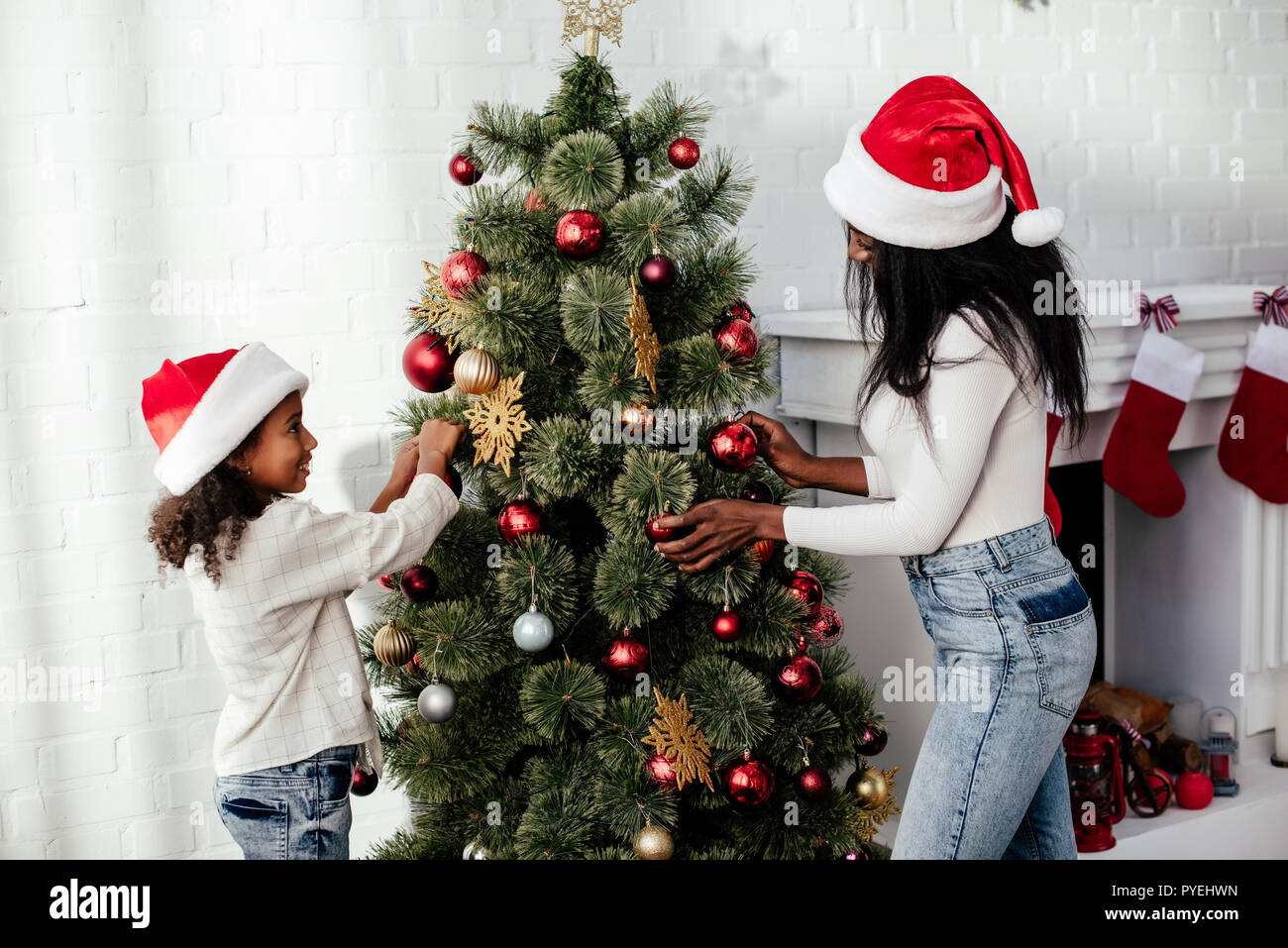 african american mother and daughter in santa claus hats decorating ...