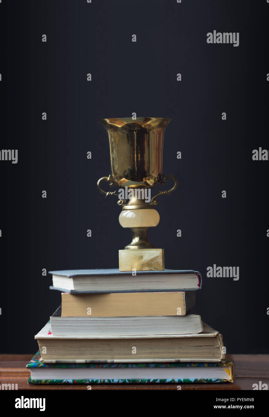 Golden trophy on pile of books, against blackboard, learning ...