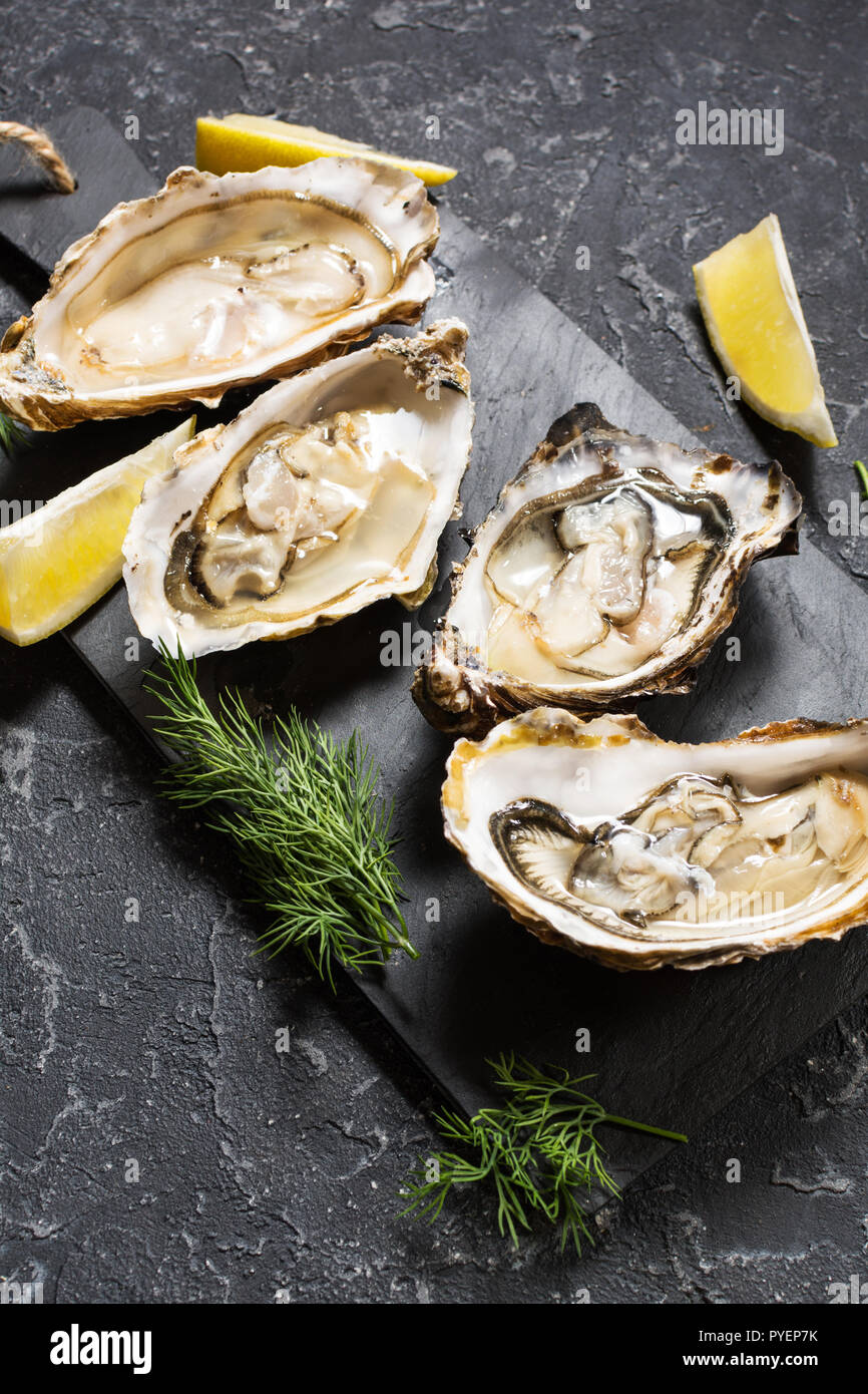 Opened Oysters with lemon on dark stone texture background Stock Photo ...