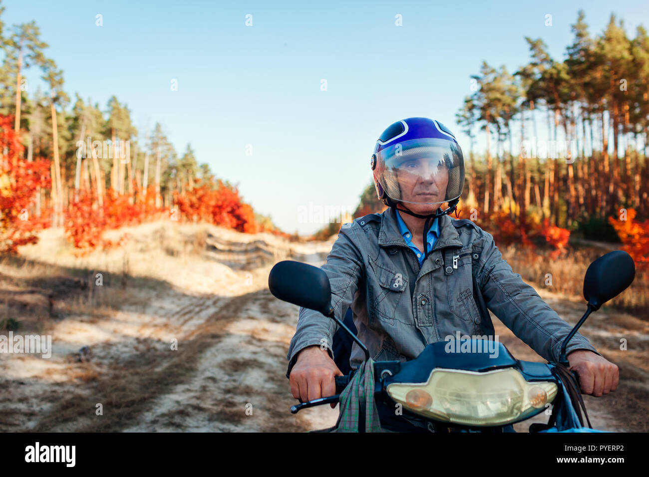 Senior man riding scooter on autumn forest road. Driver in helmet ...