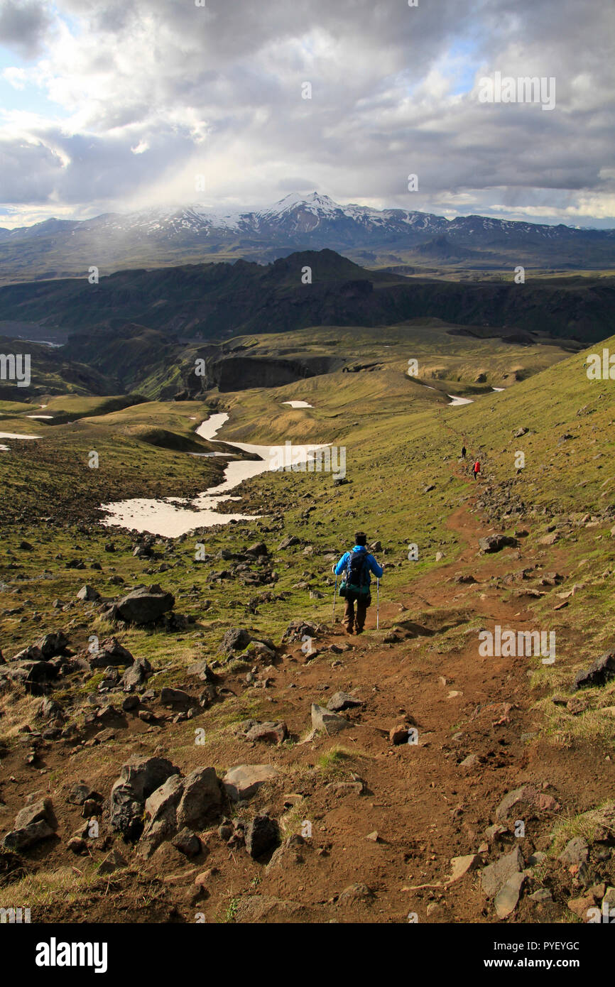 A hiking group walks down a path on a volcano with a mountain range in ...