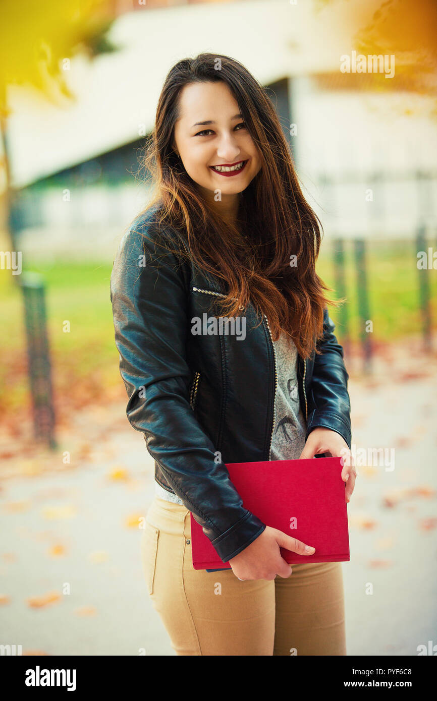 Young woman student outdoors portrait holding a red book and smile ...
