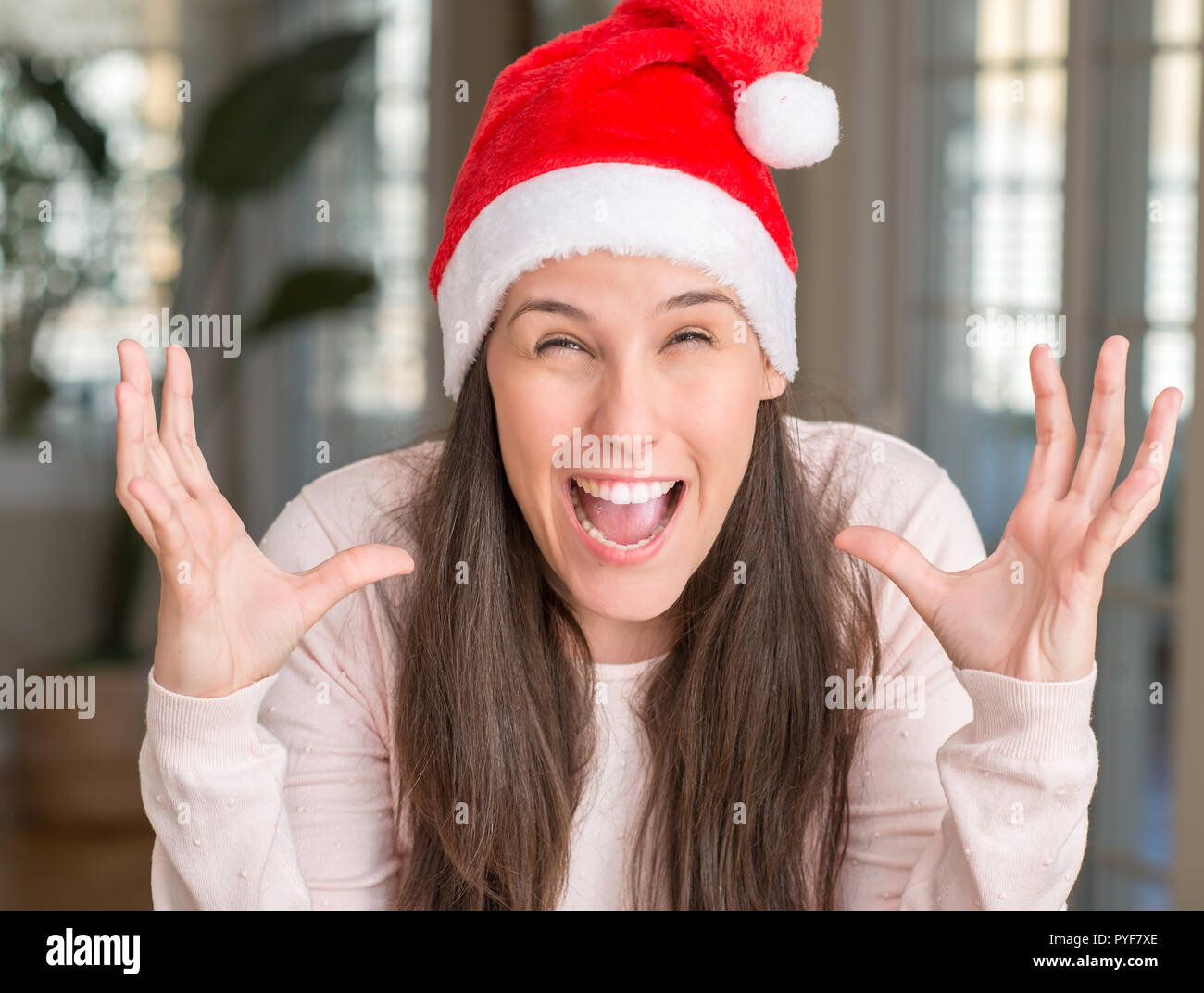 Beautiful young woman wearing Santa Claus hat at home crazy and mad ...