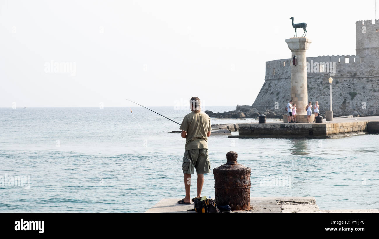 A lone fisherman fishing at the entrance to the harbour in Rhodes town ...