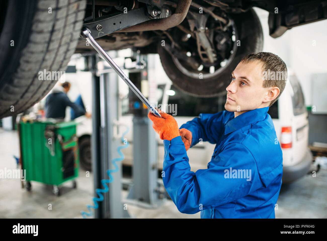 Repairman with a wrench checks the suspension, car on the lift ...