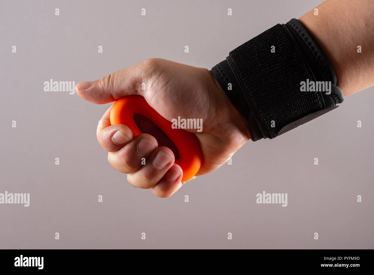 hand with a wrist protective strap doing exercises by squeezing an O ...