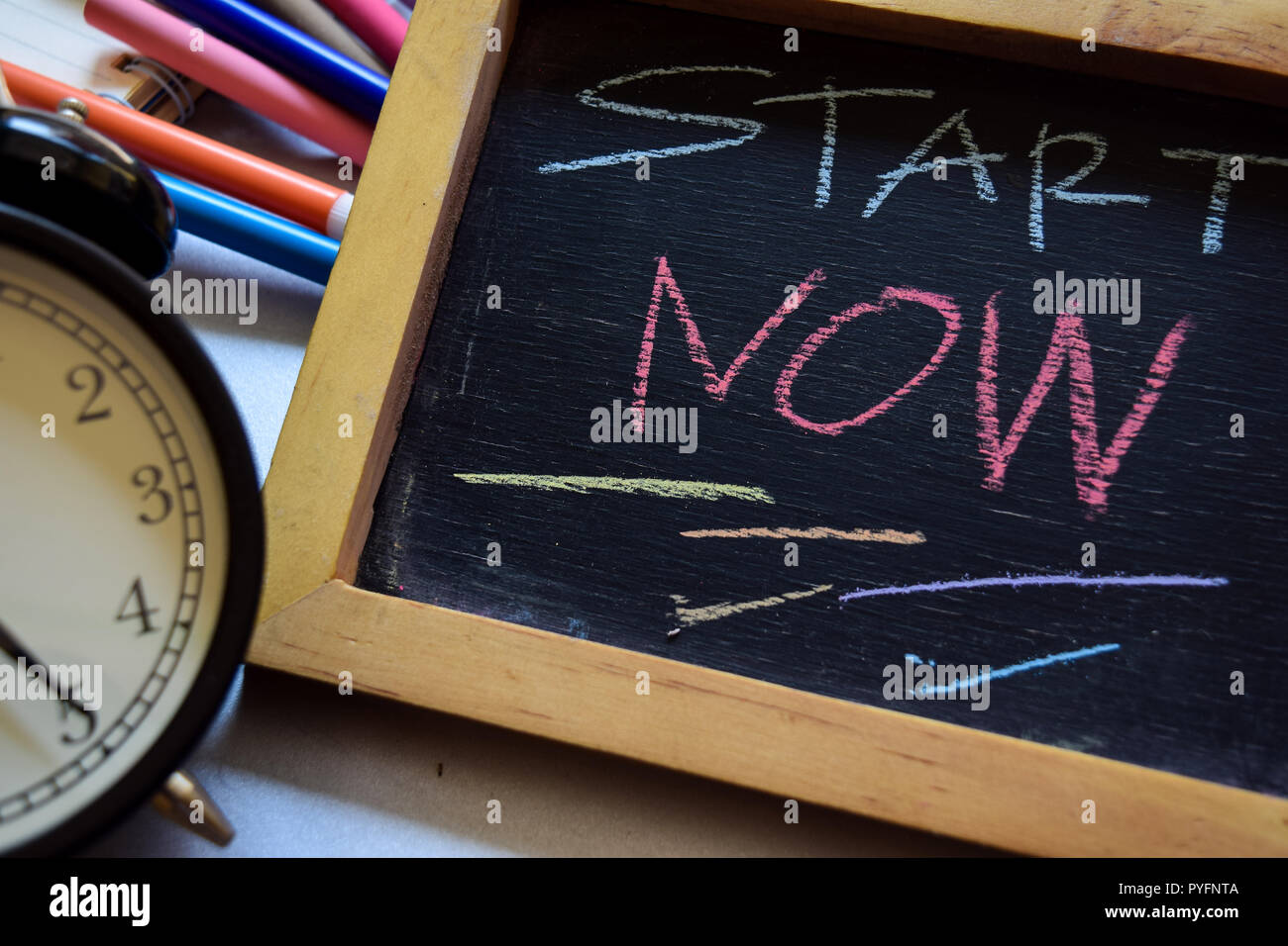 Start now phrase colorful handwritten on chalkboard, alarm clock with ...
