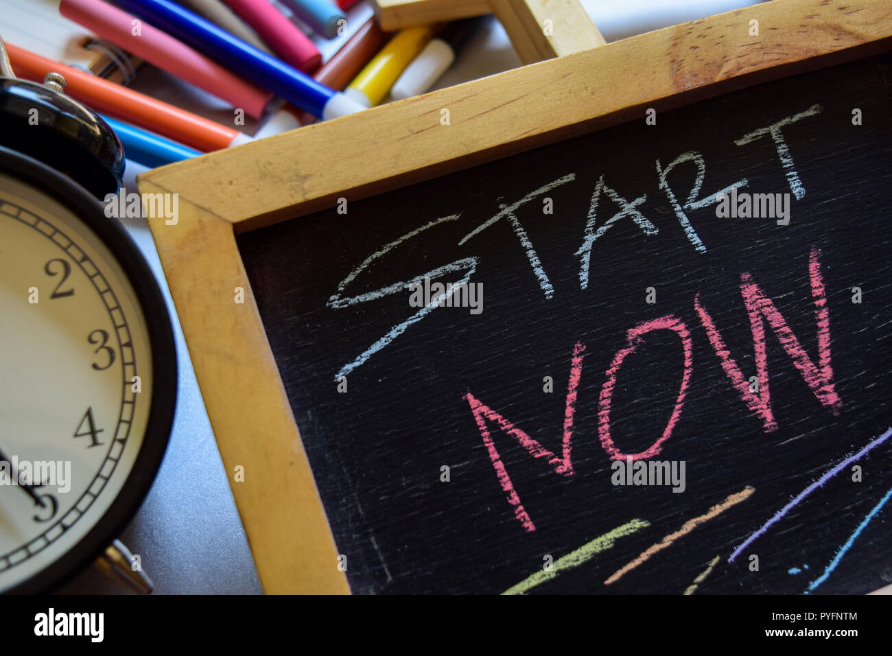 Start now phrase colorful handwritten on chalkboard, alarm clock with ...