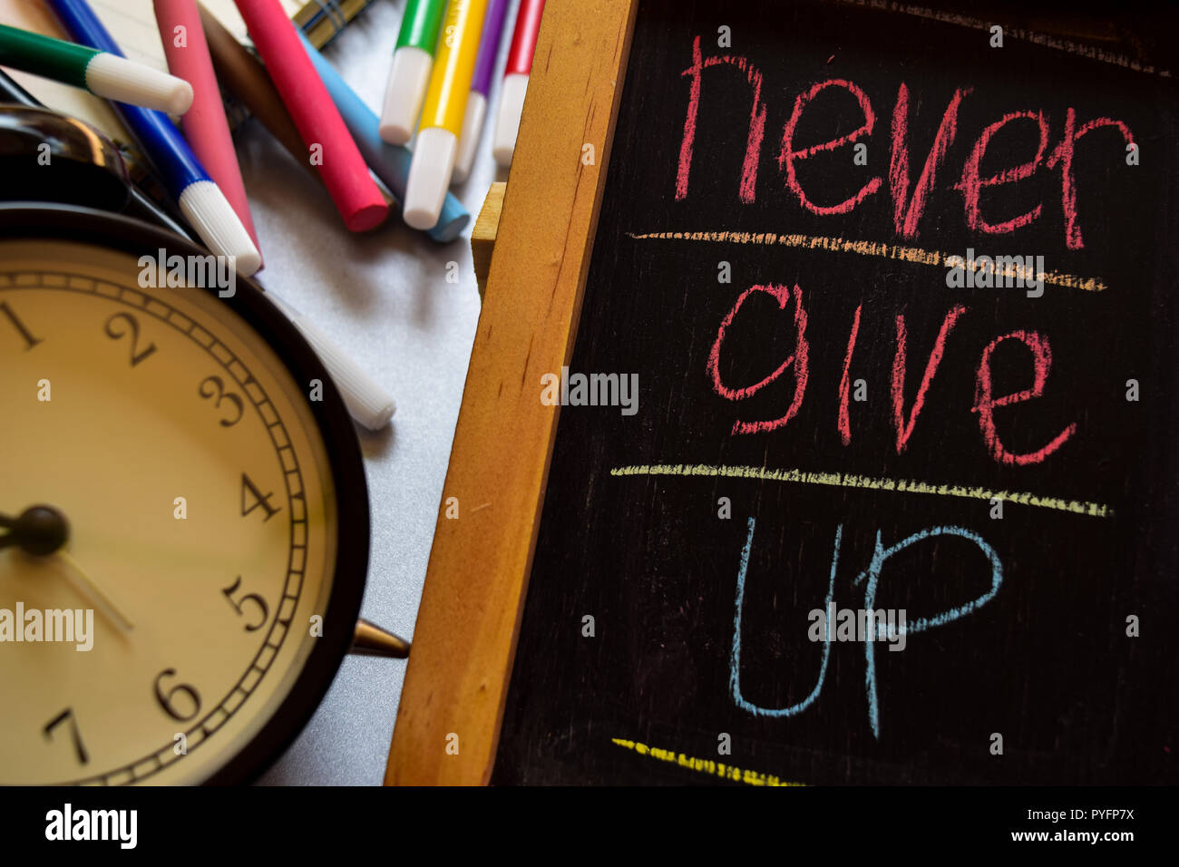 Never give up on phrase colorful handwritten on chalkboard, alarm clock ...