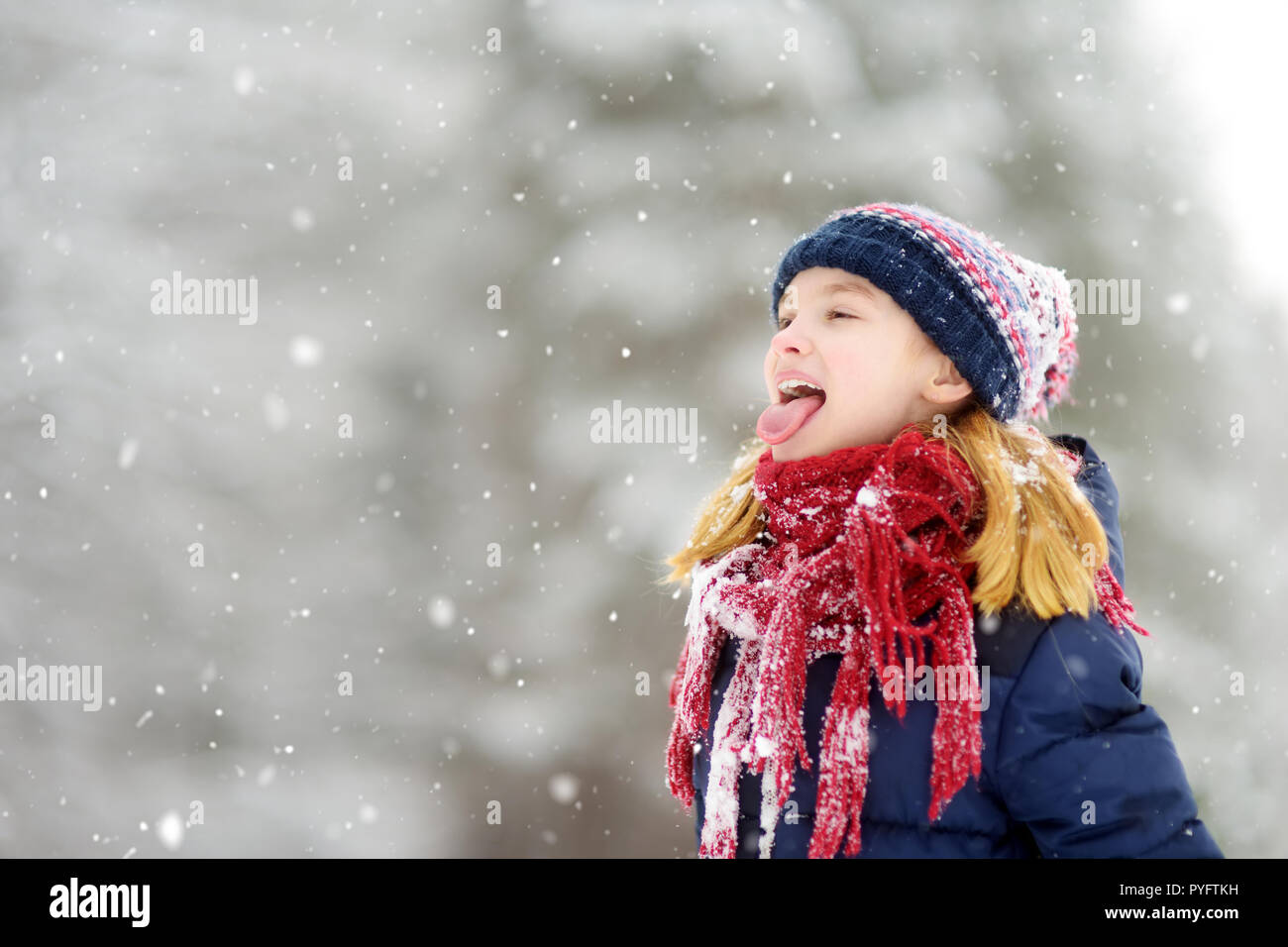 Adorable little girl catching snowflakes with her tongue in beautiful ...