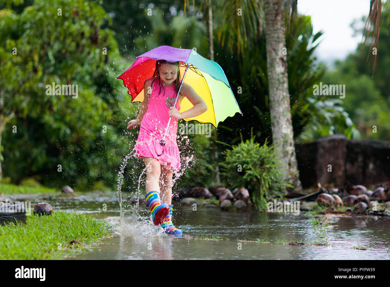 Kid playing out in the rain. Children with umbrella and rain boots play ...