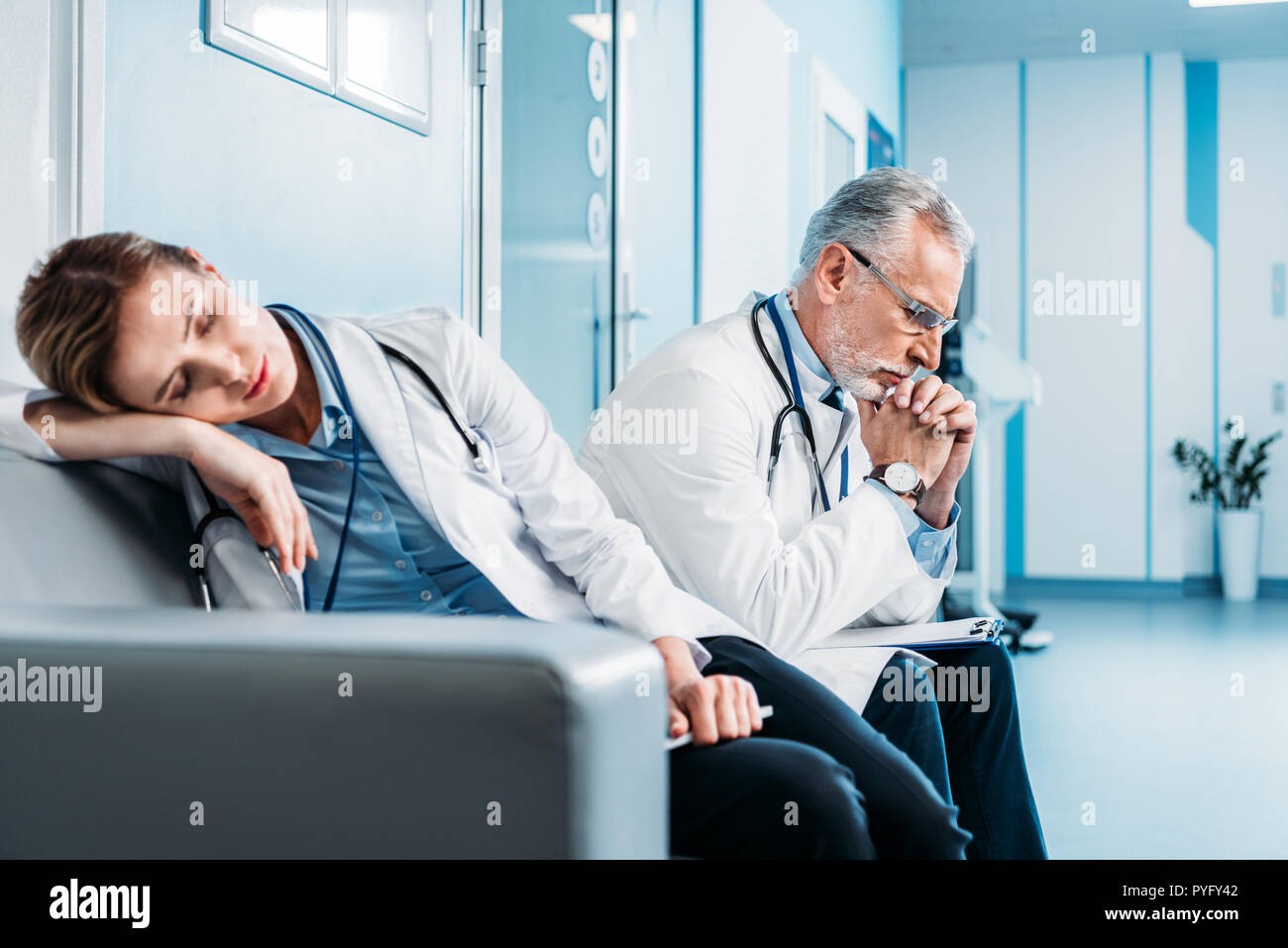 female doctor sleeping on couch while her male colleague sitting behind ...