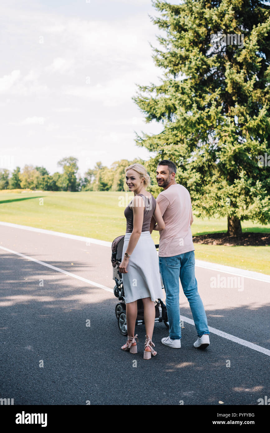 parents walking with baby carriage on road in park and looking at ...