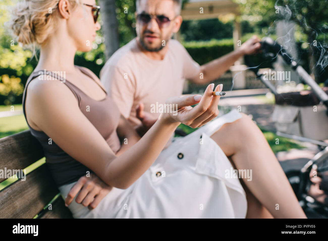 mother smoking cigarette near baby carriage in park, angry father ...