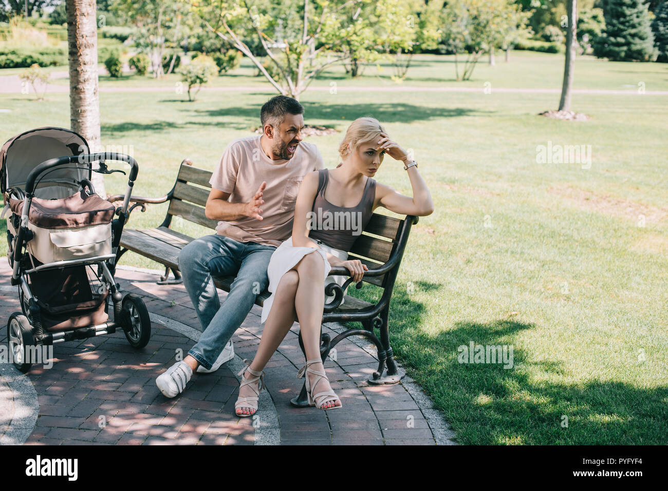 husband yelling at wife and sitting on bench near baby carriage in park ...