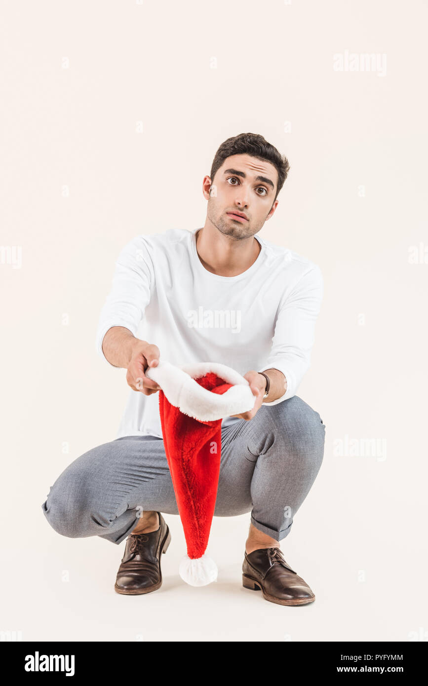 young man holding santa hat and begging isolated on beige Stock Photo ...