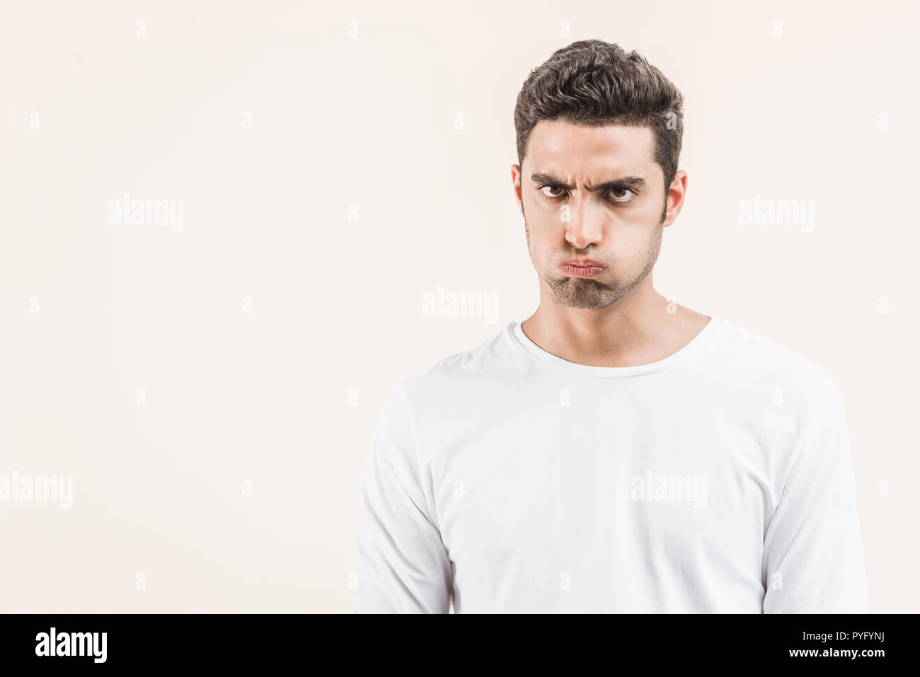 angry young man blowing cheeks and looking at camera isolated on beige ...