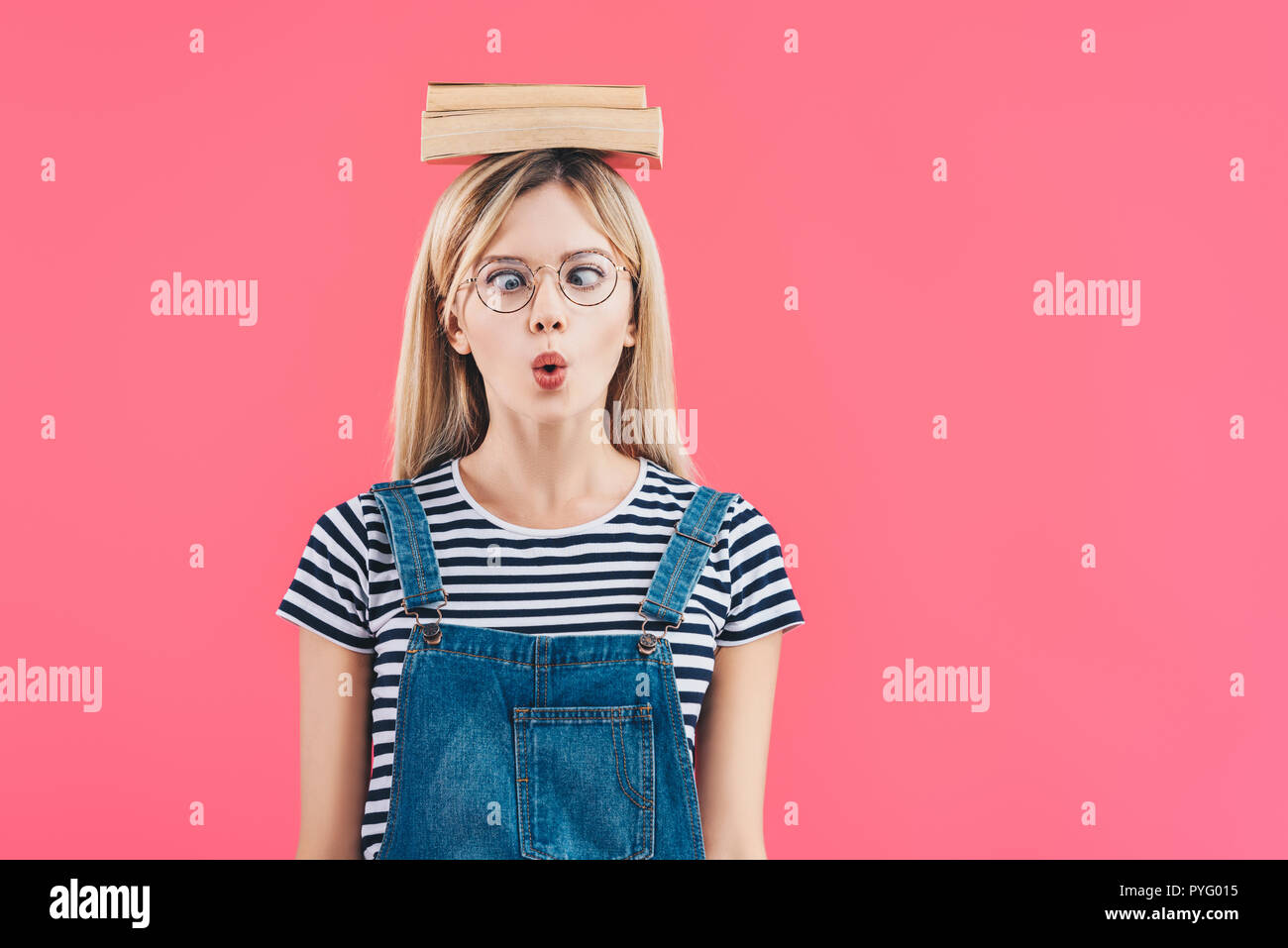 portrait of young grimace student in eyeglasses with books on head ...