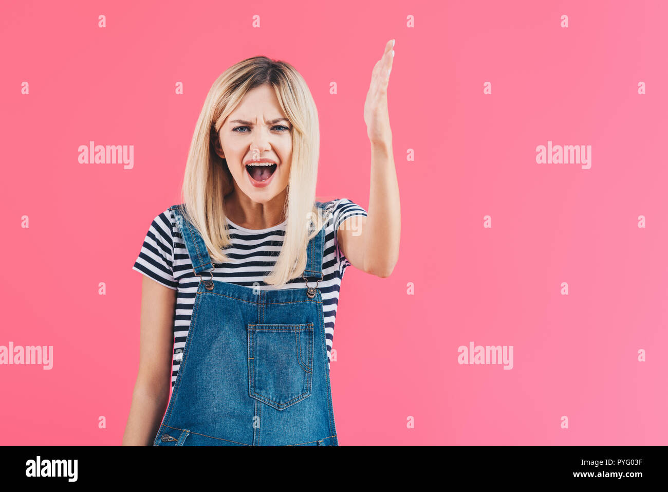 angry girl in denim overall yelling and gesturing isolated on pink ...
