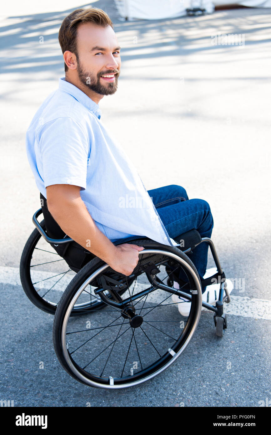 handsome smiling man using wheelchair on street and looking at camera ...