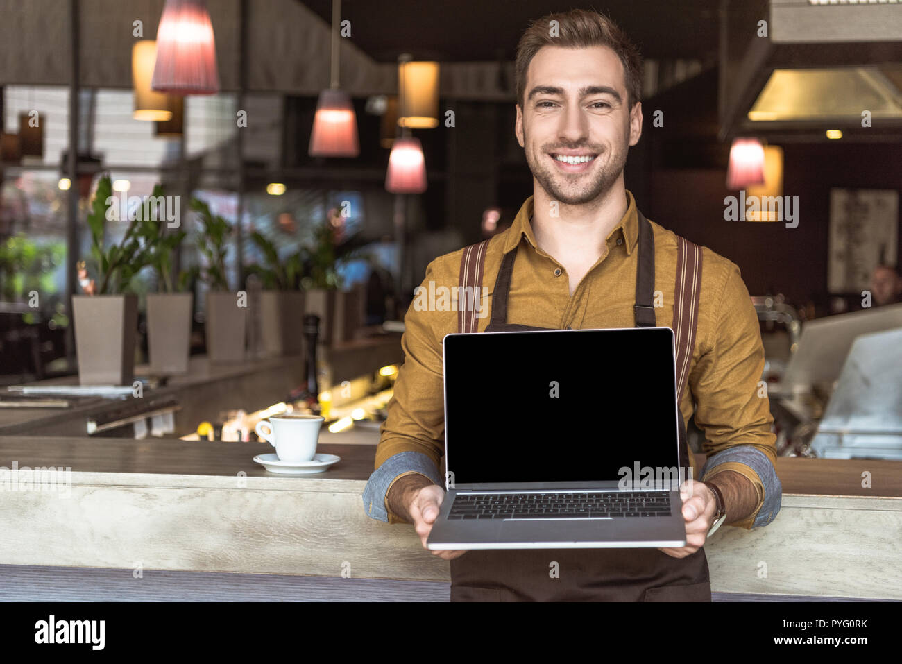 happy young waiter holding laptop with blank screen in cafe Stock Photo ...