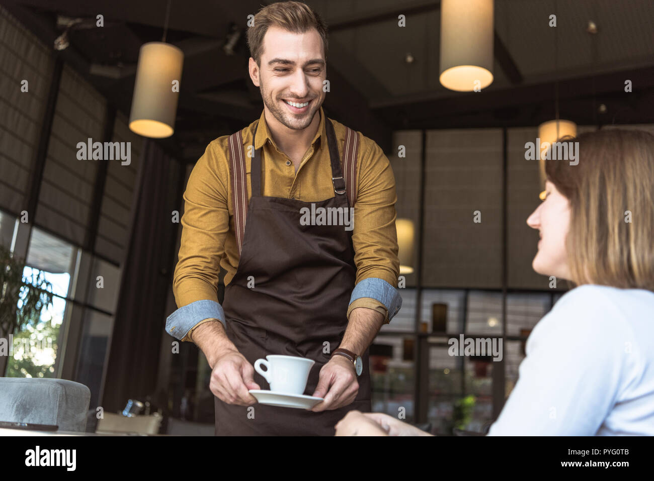 happy young waiter serving cup of coffee for female client at cafe ...